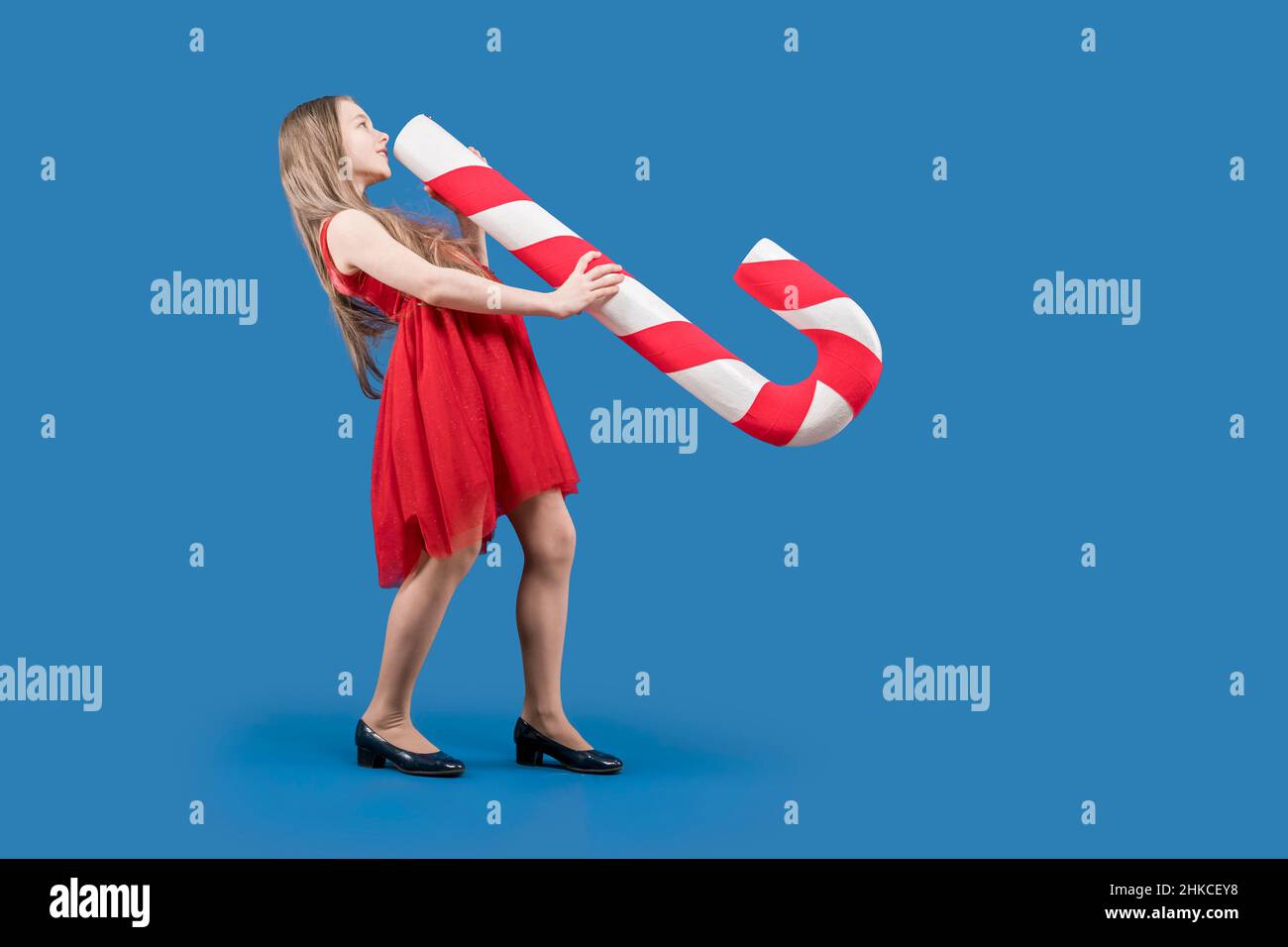 A beautiful little girl holding a huge candy in her hands on a blue ...