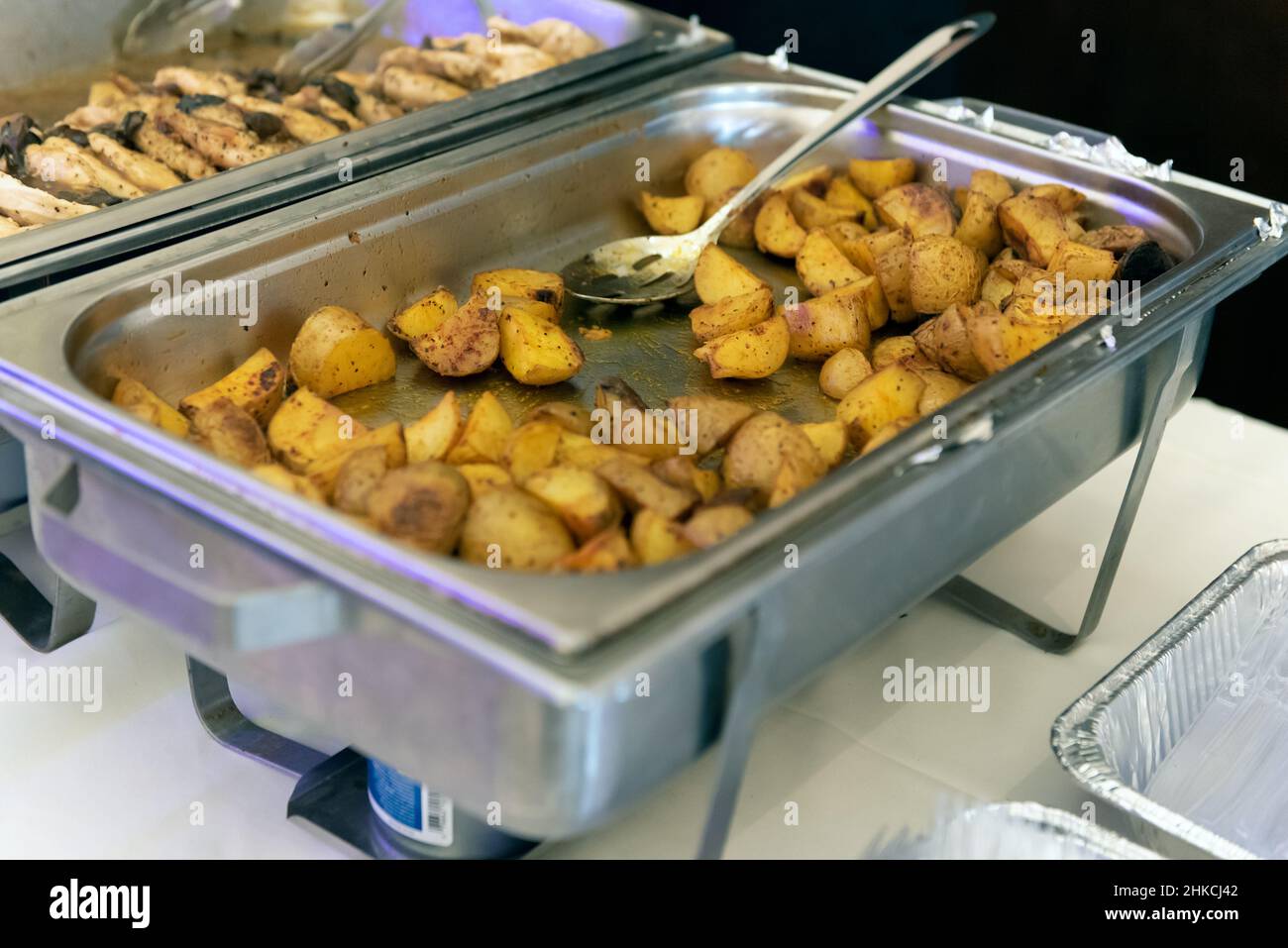Buffet table has a chaffing dish of seasoned and roasted potatoes for ...