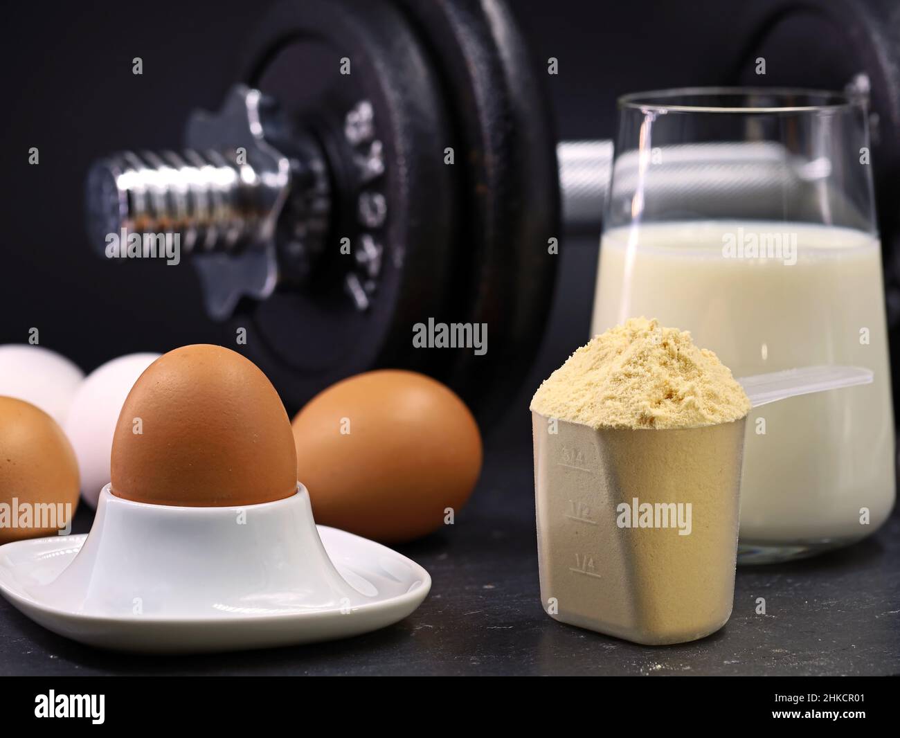eggs, scoop of whey protein powder, glass of milk and dumbbell on black ...