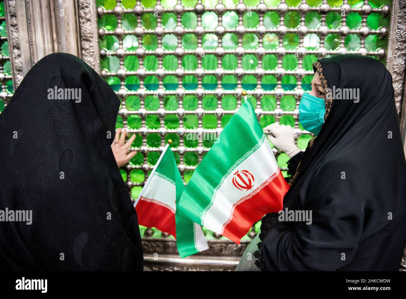 A veiled woman wearing a protective face mask holds an Iranian flag as ...