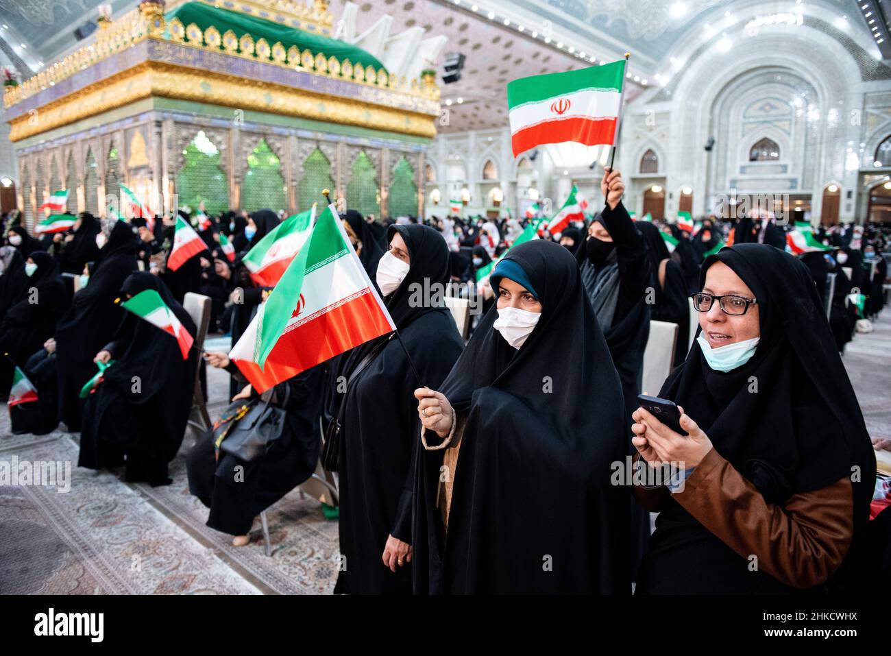 Veiled women wearing a protective face mask hold an Iranian flag while ...