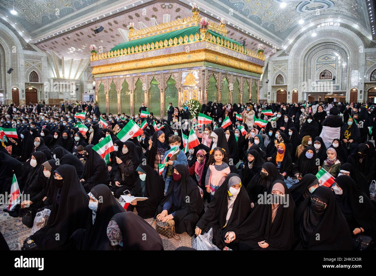 Veiled women wearing a protective face mask hold an Iranian flag while ...