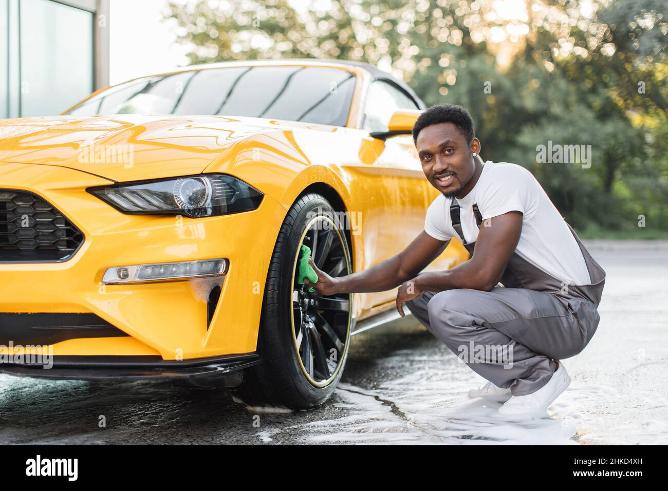 Car washing on open air. Young guy in gray overalls African bearded man ...