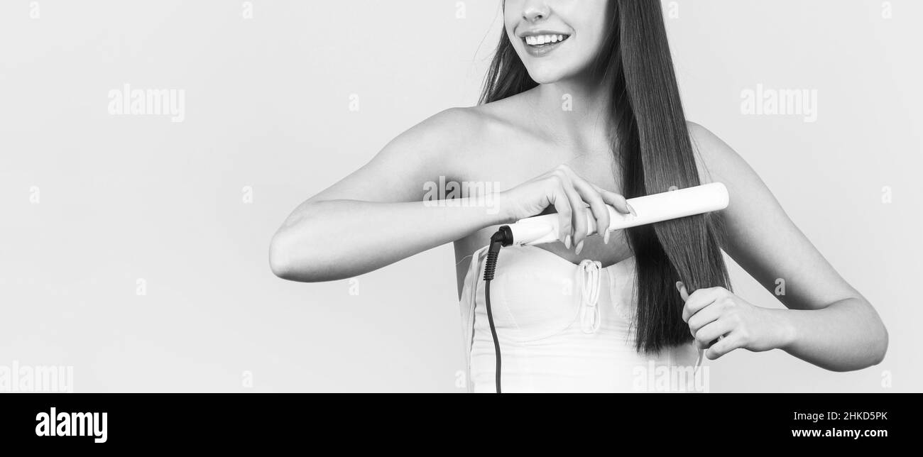 Woman straightening hair with straightener. Portrait of young beautiful ...