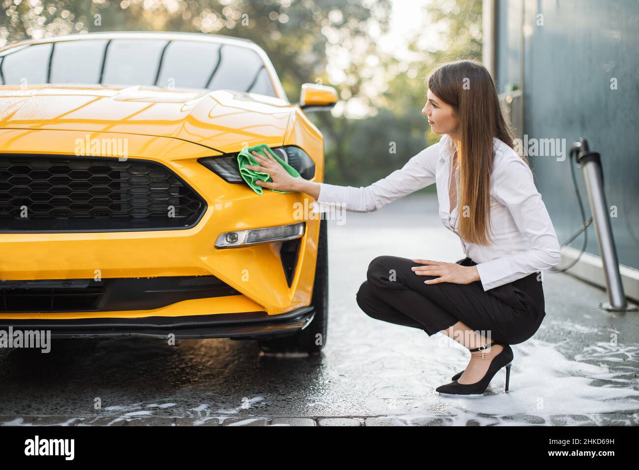 Cheerful business woman washing and wiping modern sport yellow car ...