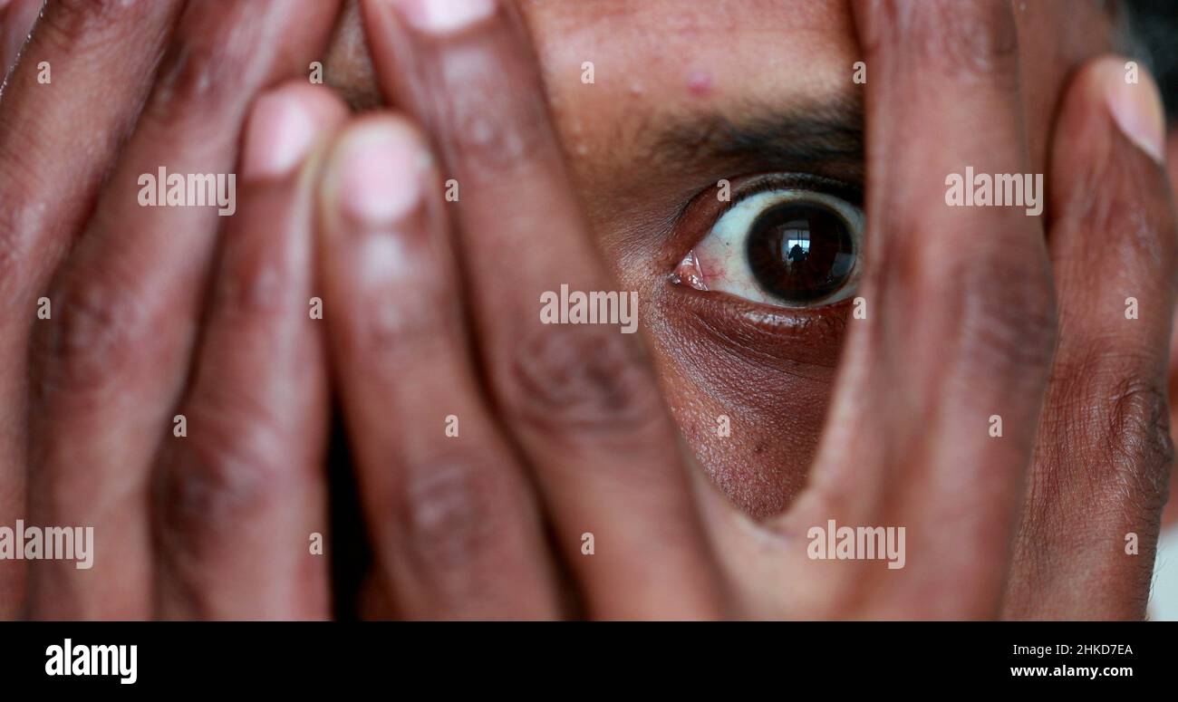 Person covering face with hands. Black man hiding behind hand scared to ...