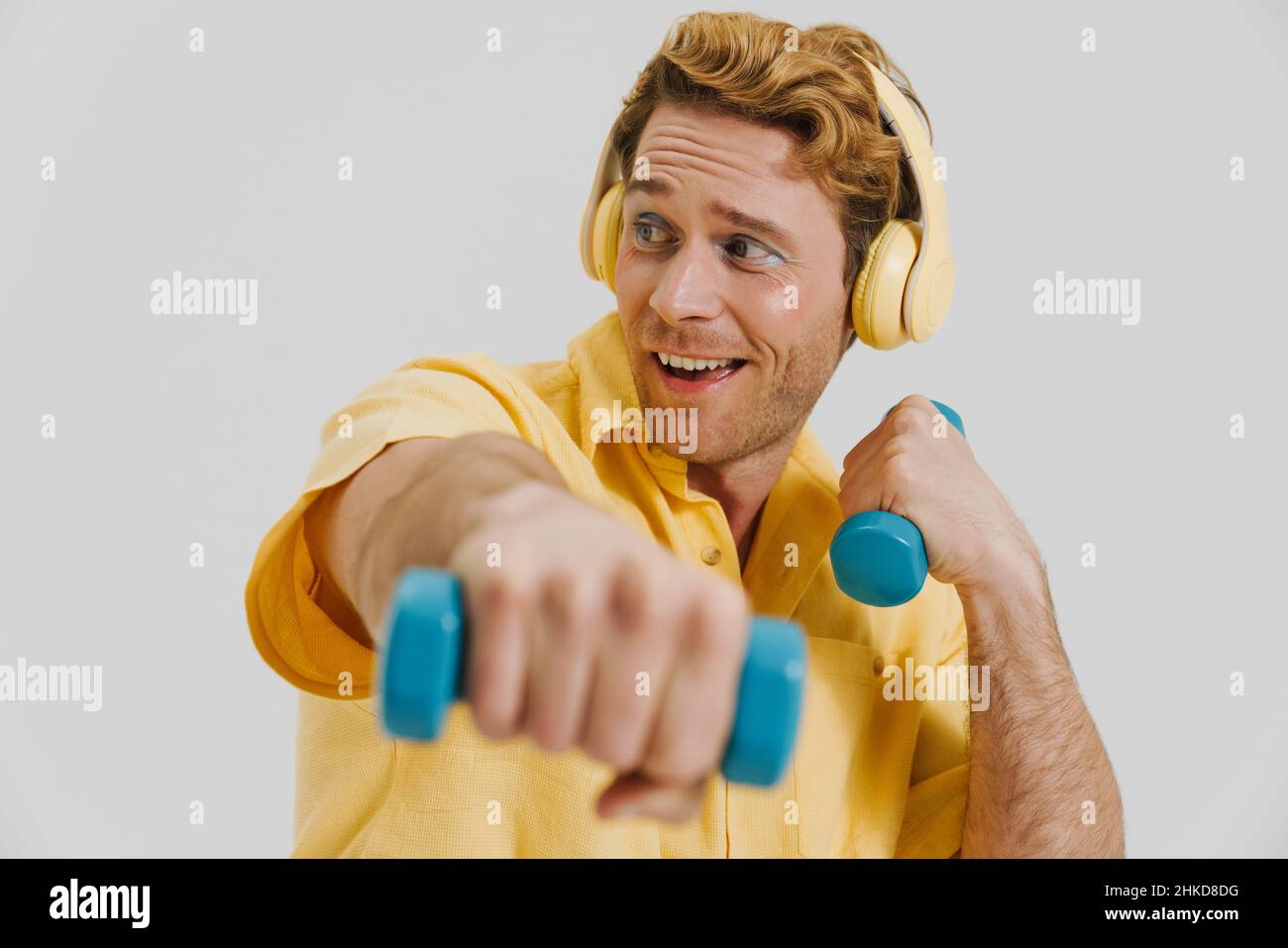 Ginger man in headphones smiling while doing exercise with dumbbells ...