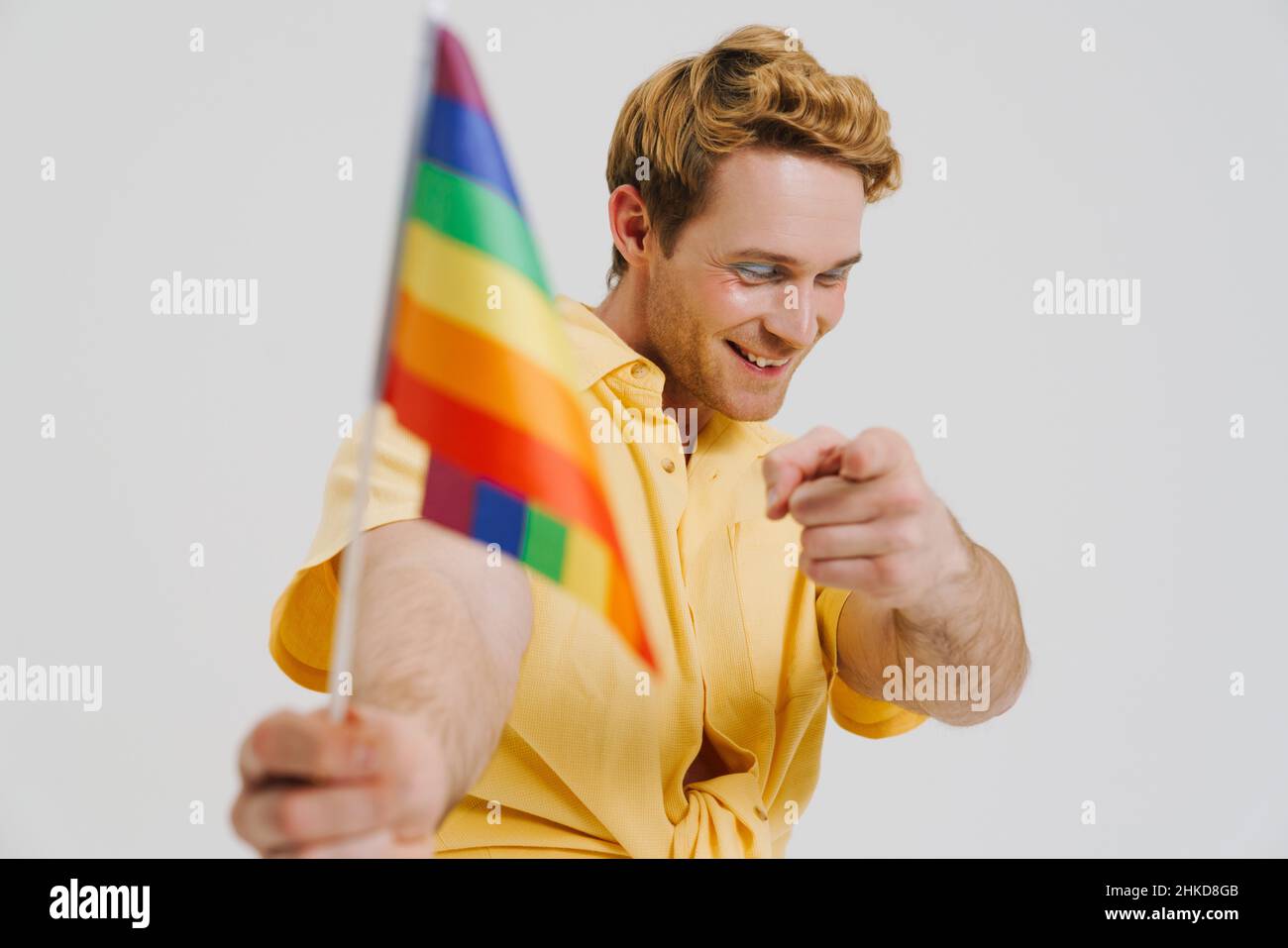 Ginger young man showing rainbow flag and pointing finger at camera ...