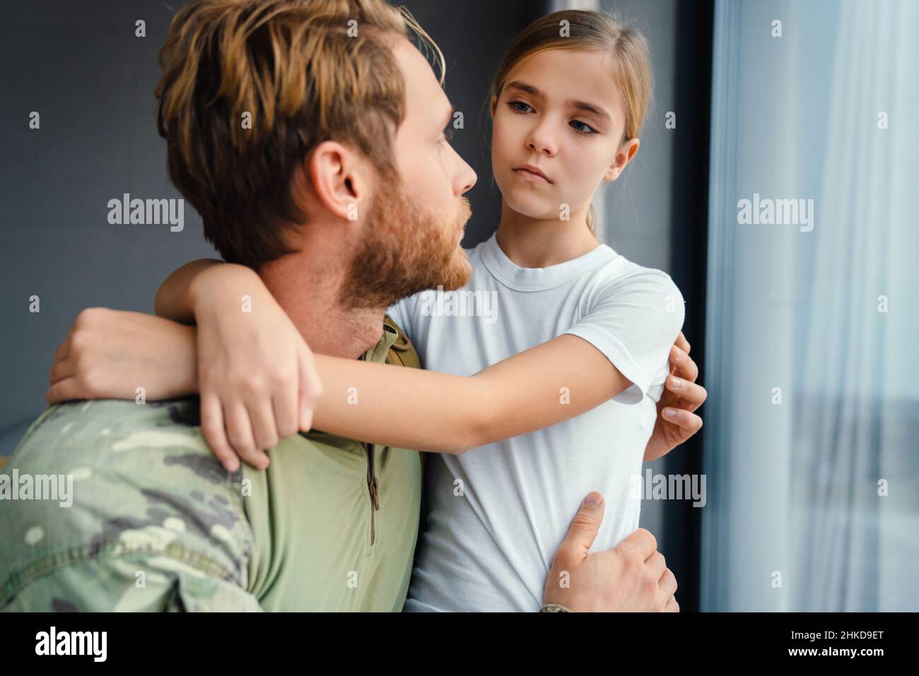 Masculine military man hugging her daughter while kneeling indoors ...