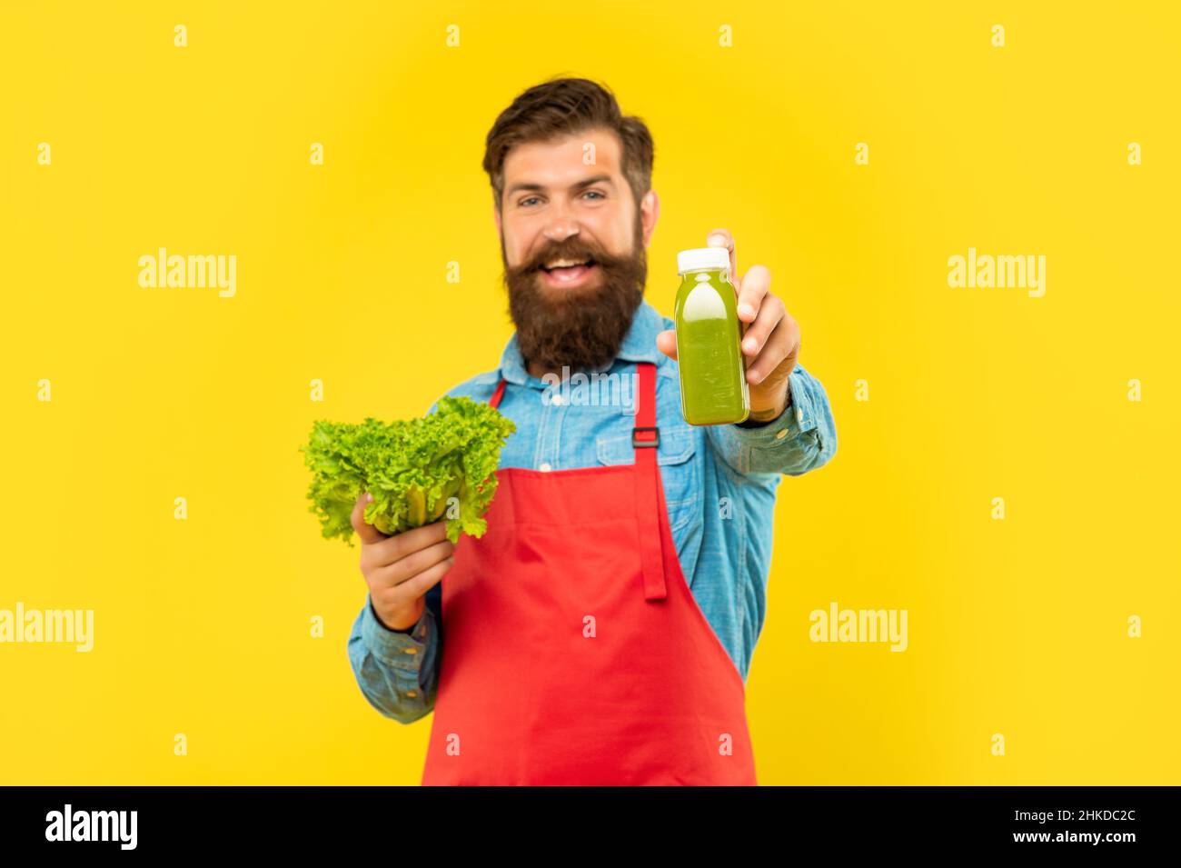 Happy man giving juice bottle holding fresh lettuce yellow background ...
