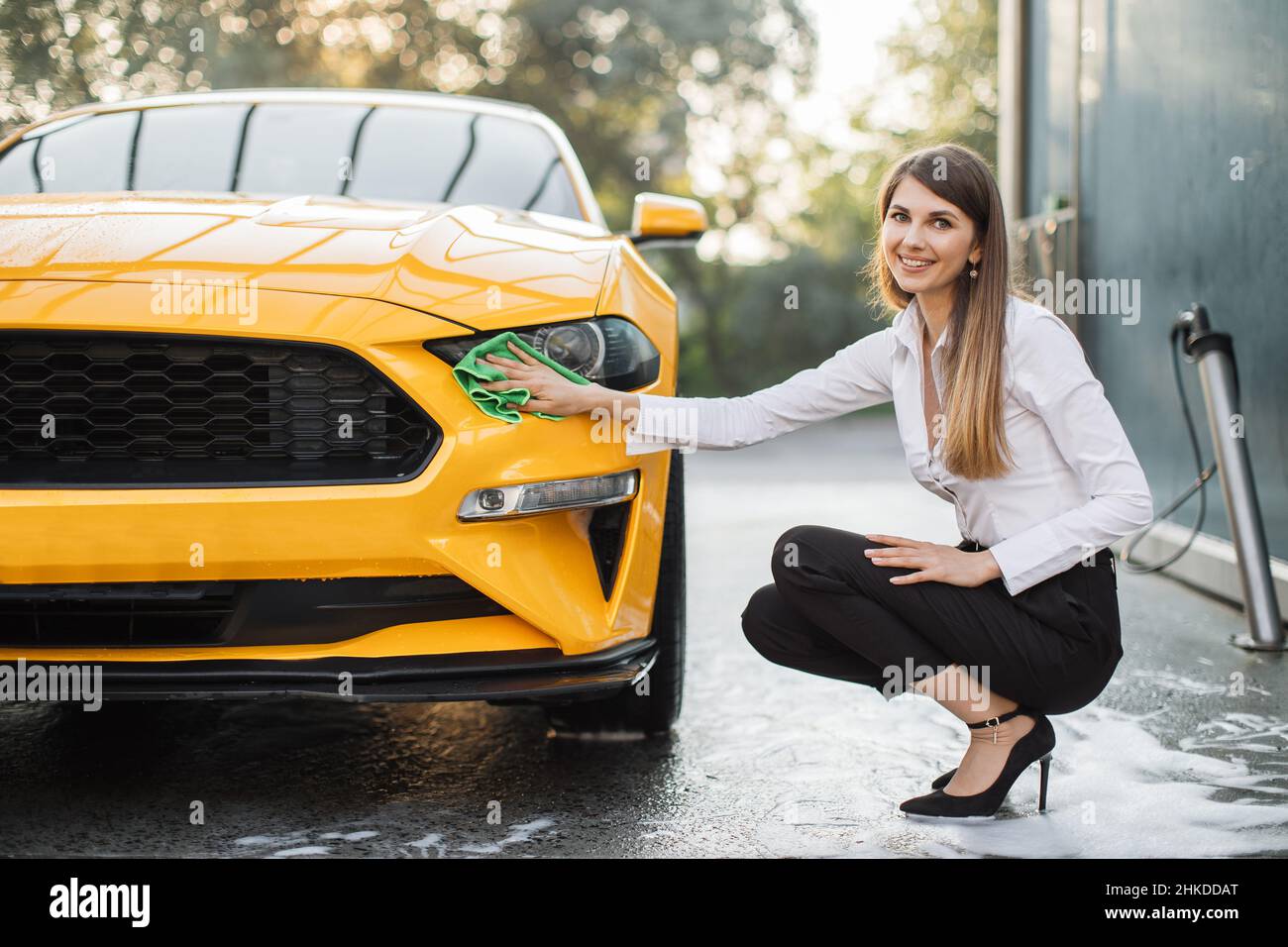 Cheerful business woman washing and wiping modern sport yellow car ...