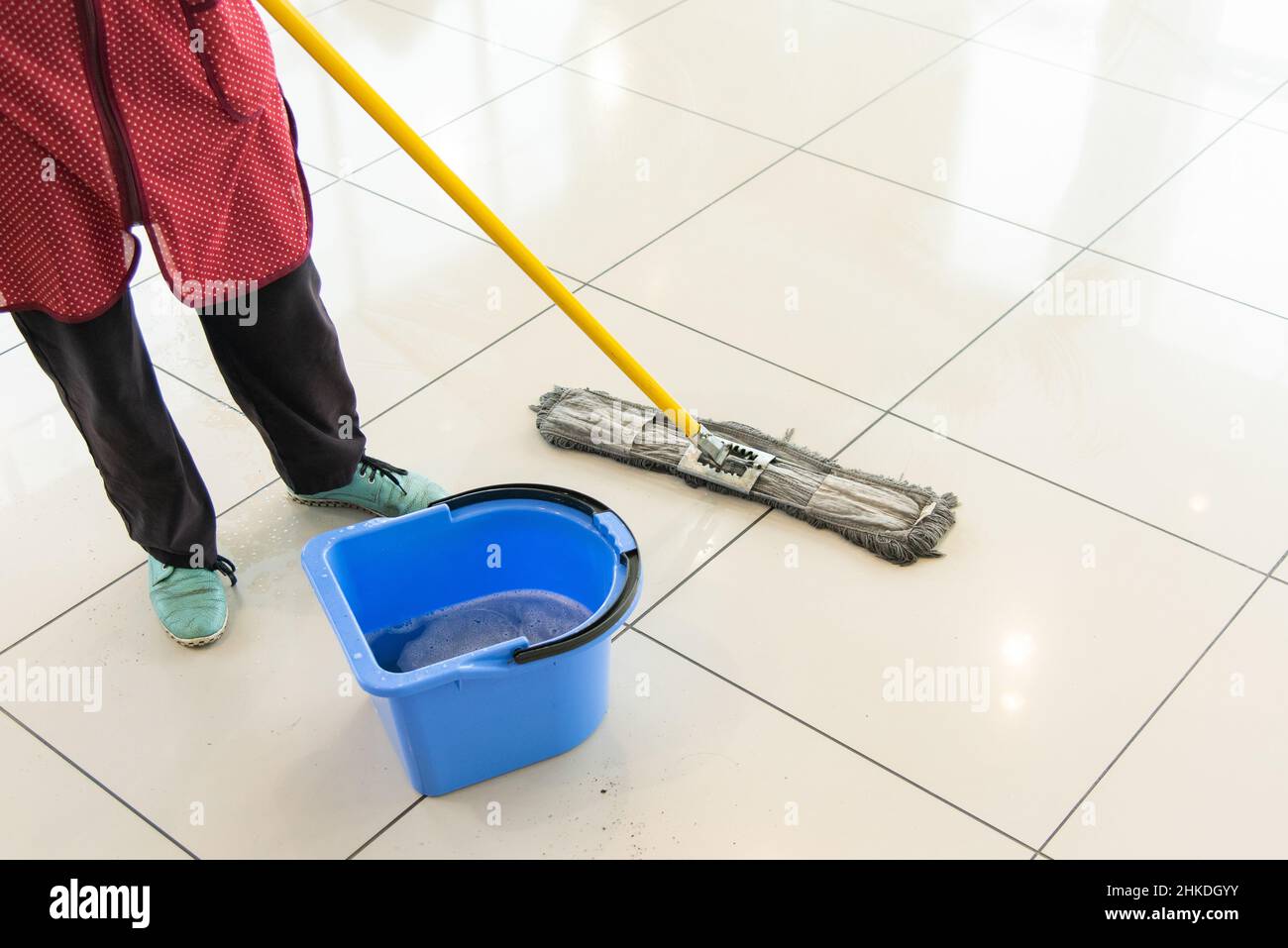 Cleaning lady washes the floor from the tiles in the mall. Woman with ...