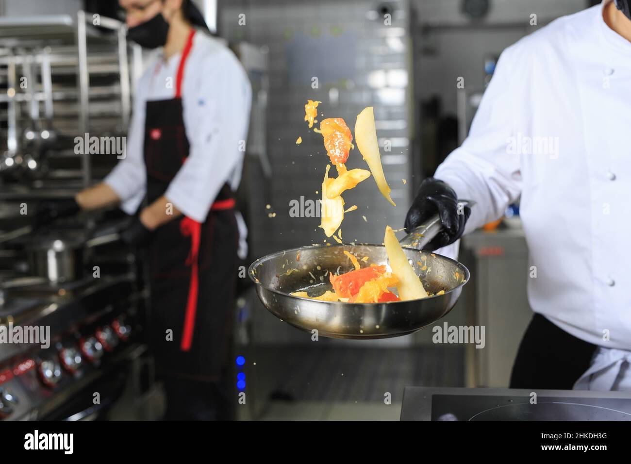 Young male chef flipping vegetables in wok at commercial kitchen Stock ...