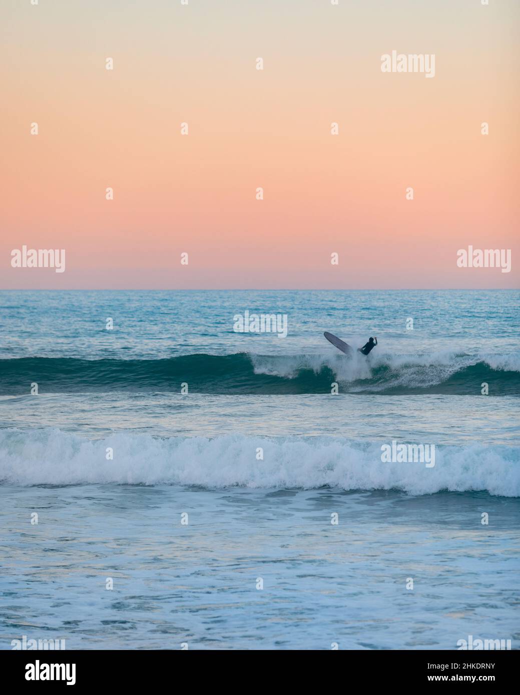 Vertical of person surfing on the ocean waves at pink sunset in Spain ...
