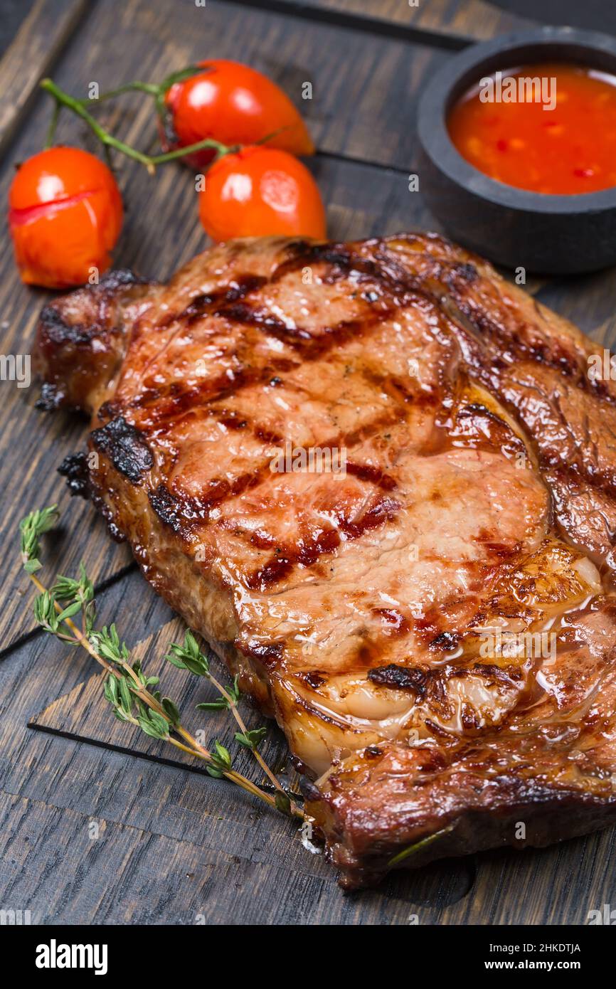 fried Rib Eye steak with cherry tomatoes and sauce on a wooden board ...