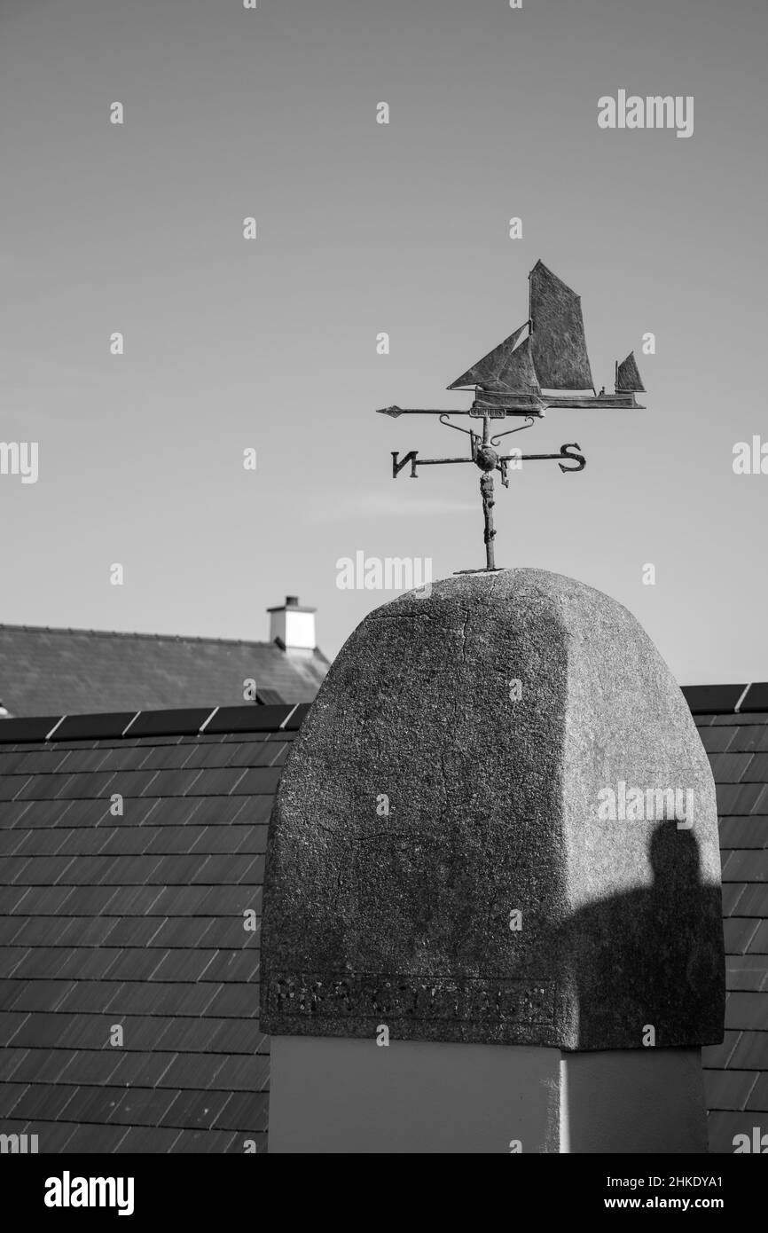 Vertical greyscale view of a wind vane on a stone near the roof of a ...