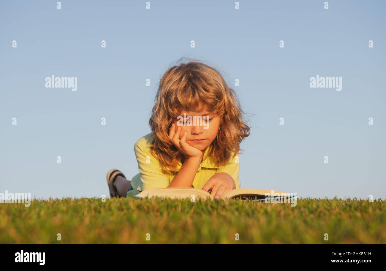 Clever child boy reading book laying on grass on grass and sky ...