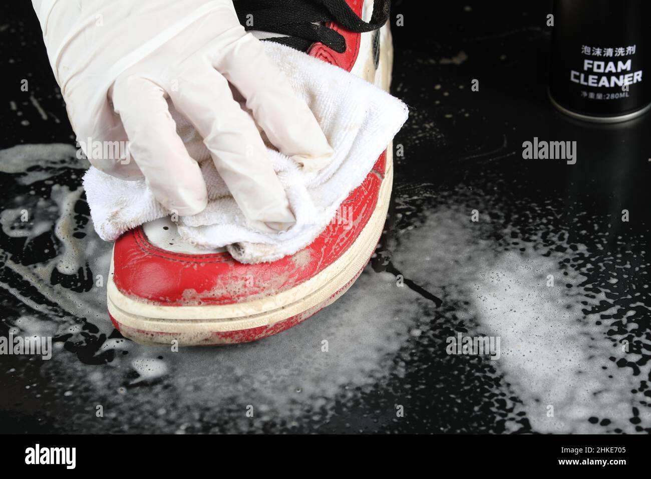 Person washing the sneakers with sneakers foam and a towel indoors ...