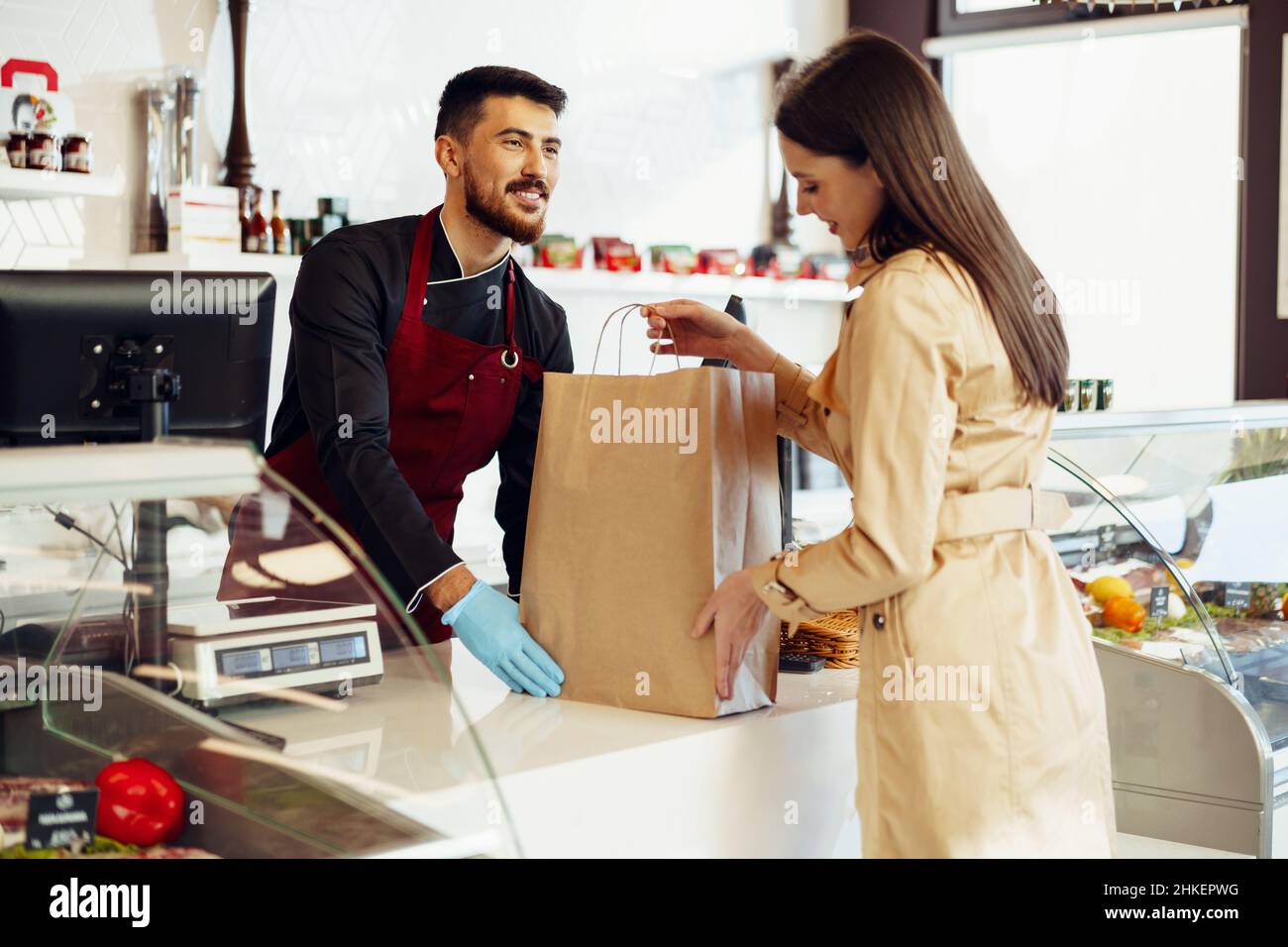 Shop assistant handling shopping bag to female customer in grocery ...