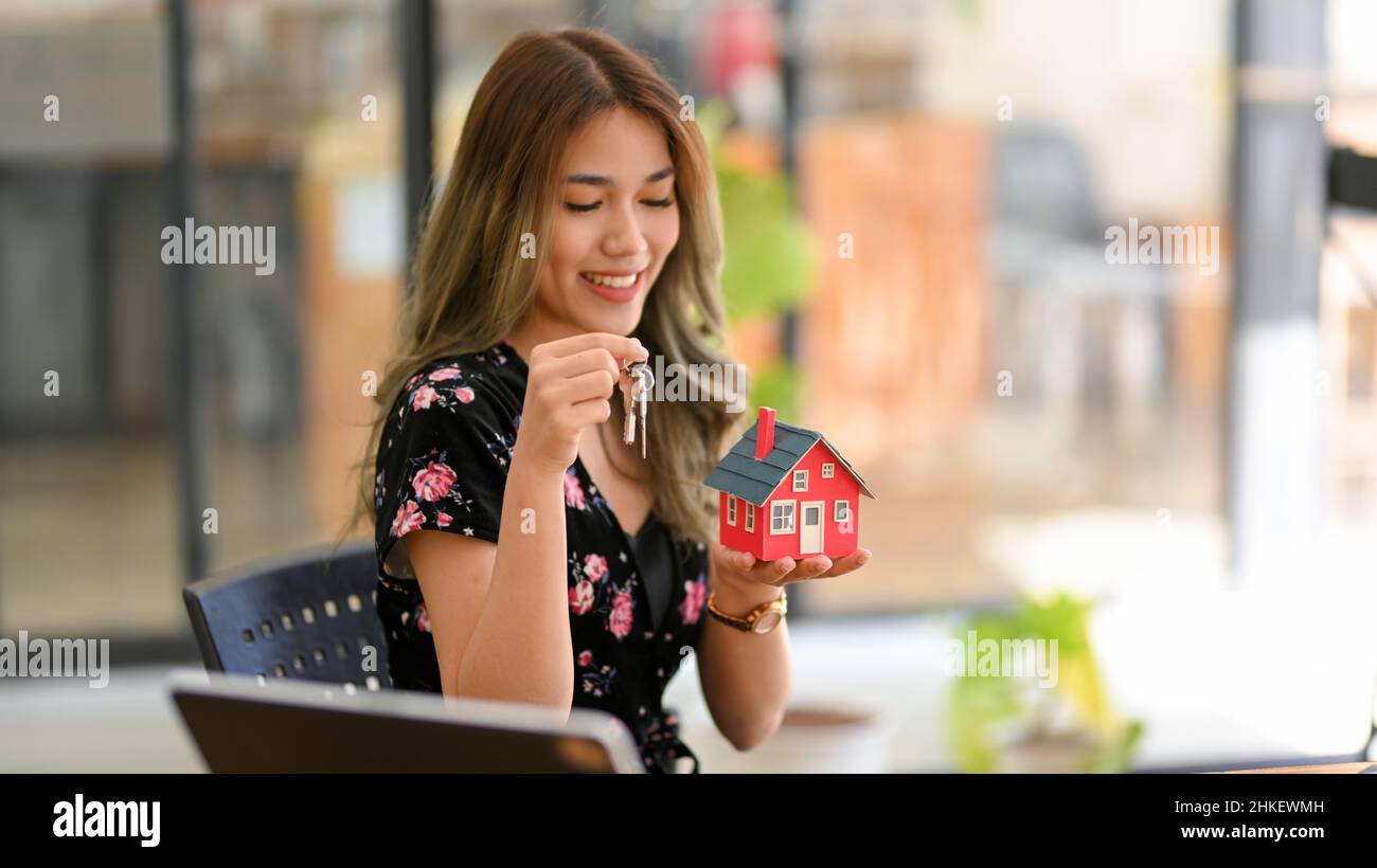 Gorgeous Asian Young Real Estate Agent Holding A Stylish House Model And House Key At Her Office