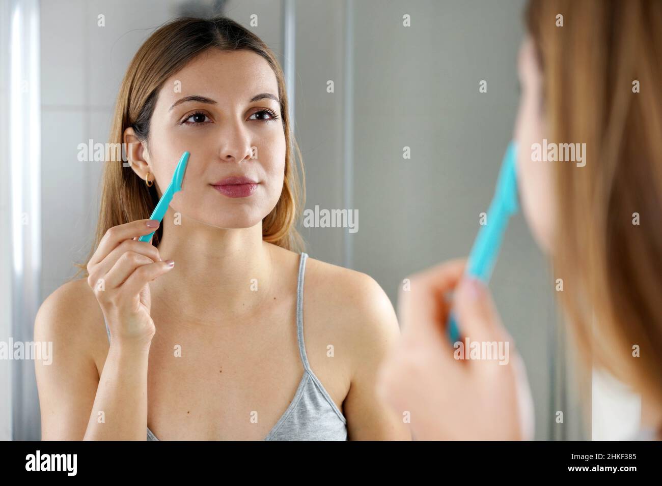 Beautiful young woman shaving her face by razor at home. Pretty woman ...