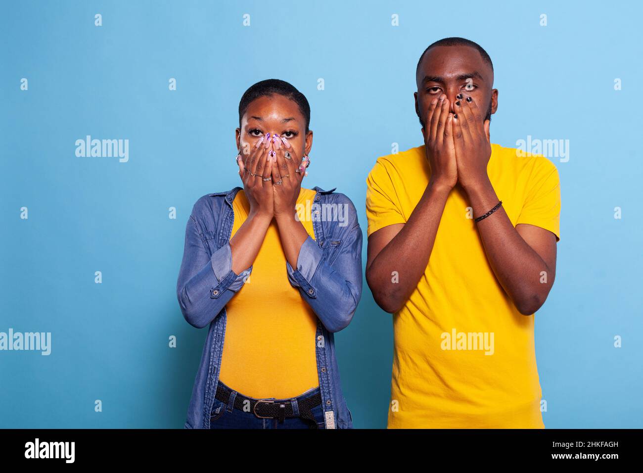 Stupefied boyfriend and girlfriend covering open mouth in studio ...