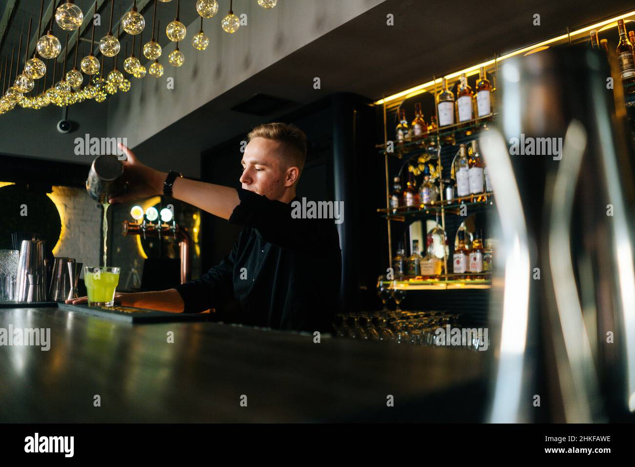 Side low-angle view of barman pouring fresh alcoholic drink into ...