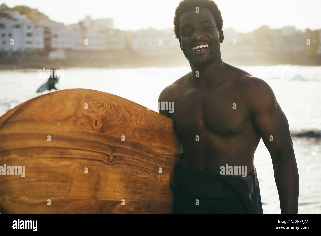 African surfer man holding vintage surf board on the beach at sunset ...