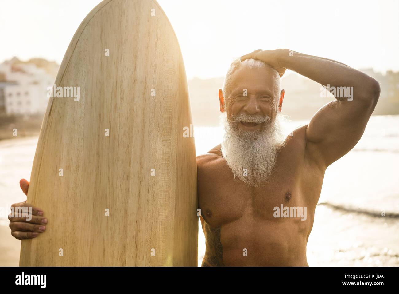 Fit senior surfer holding vintage surf board on the beach at sunset ...