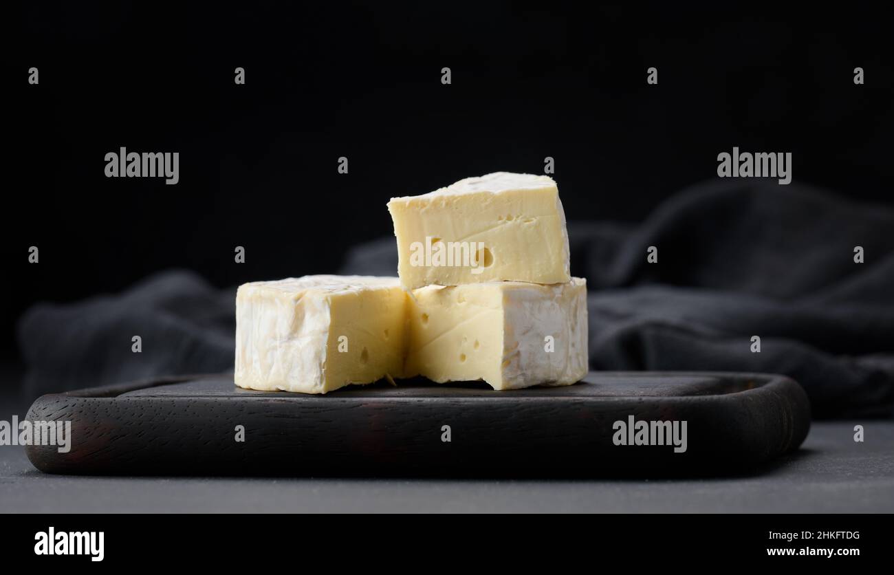 round brie cheese on brown wooden cutting board, black background Stock ...