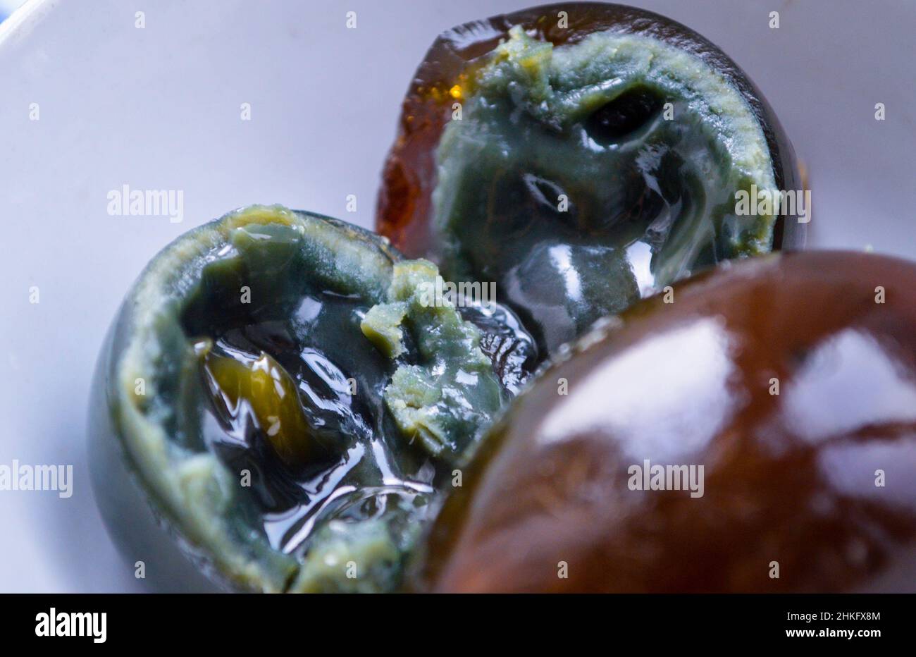 Closeup of Chinese century eggs in white bowl. The black egg is cut in ...