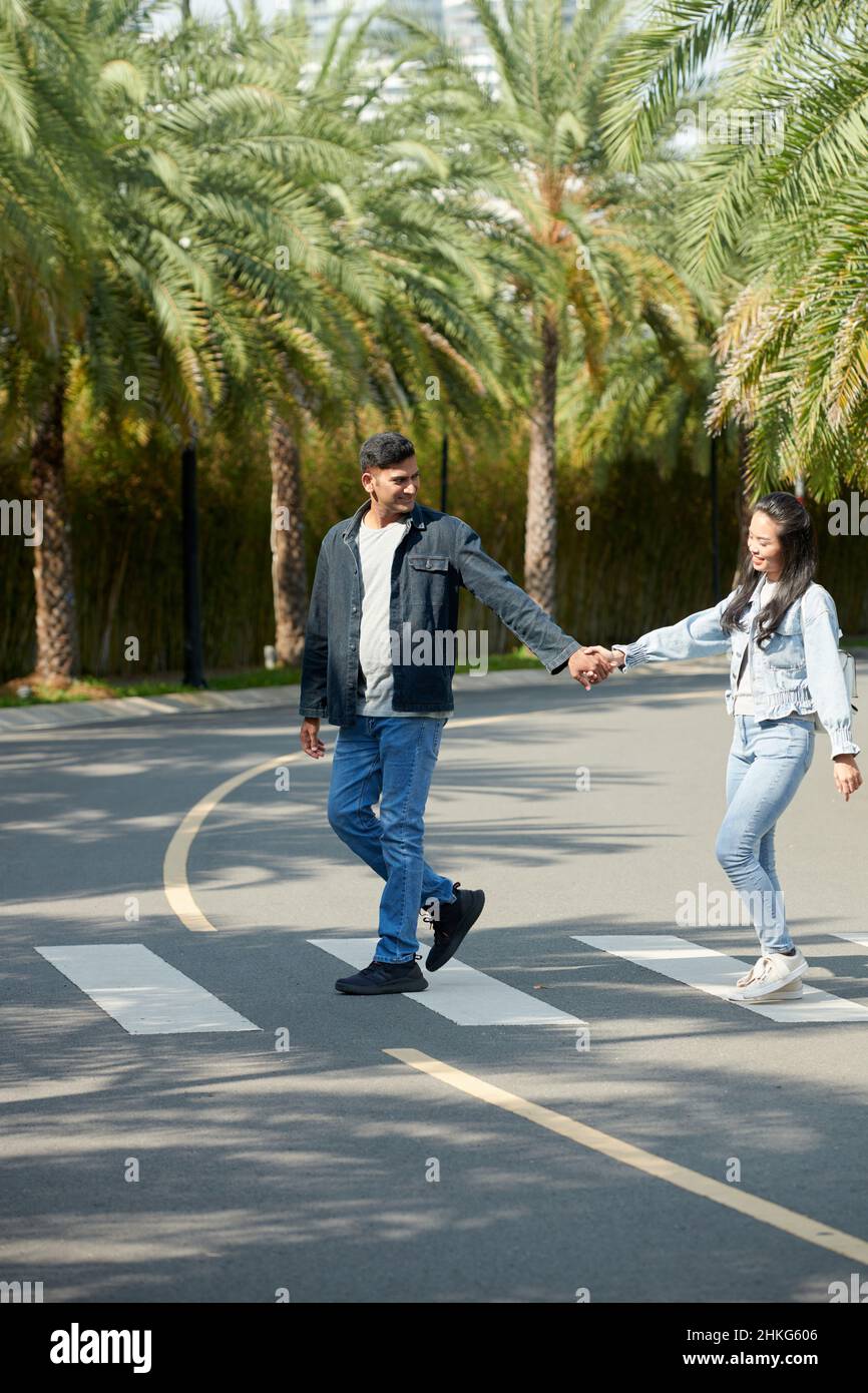 Positive young couple holding hands when crossing road Stock Photo - Alamy