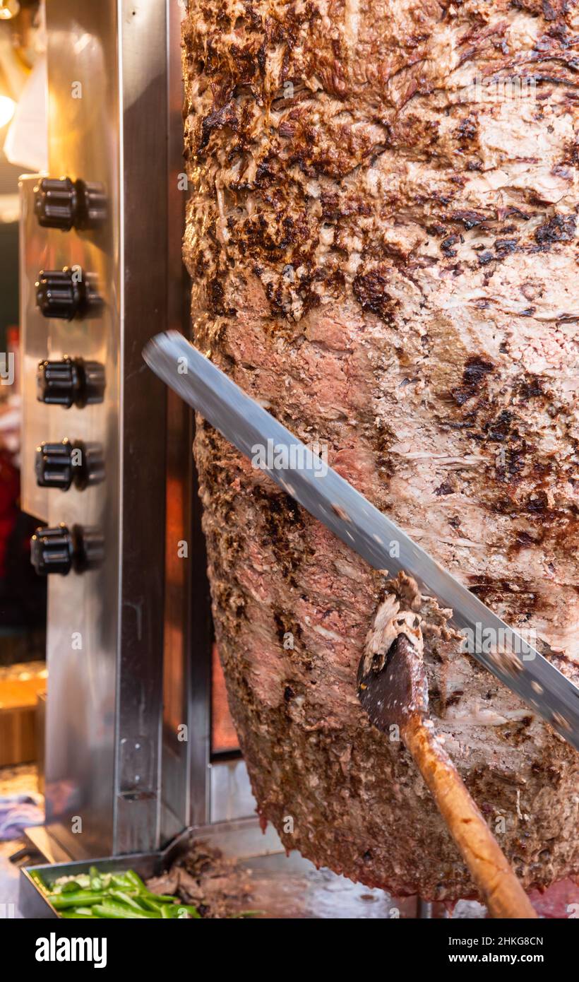 Chef cutting grilled lamb meat from rotating spit making traditional ...
