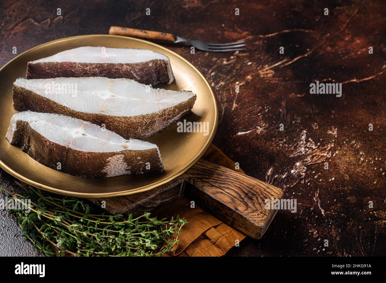Sliced halibut fish, raw steaks on plate with thyme. Dark background ...