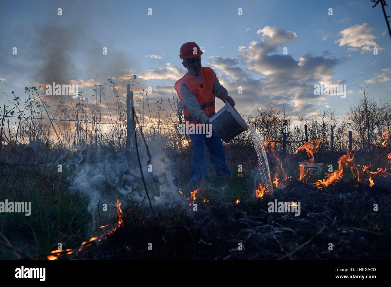 Fireman ecologist extinguishing fire in field with evening sky on ...