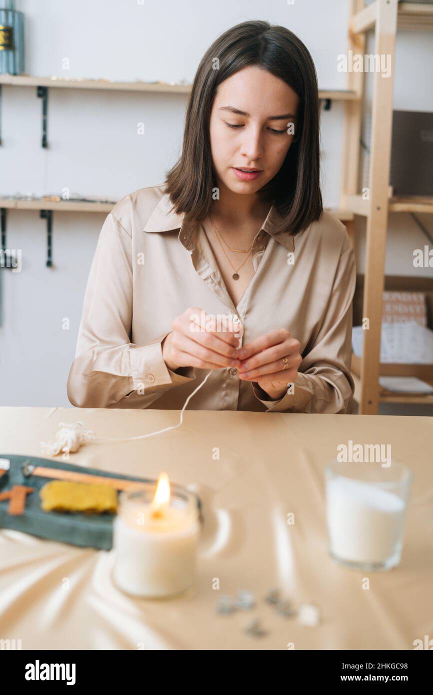 Vertical portrait of focused young woman putting thread through eye of ...