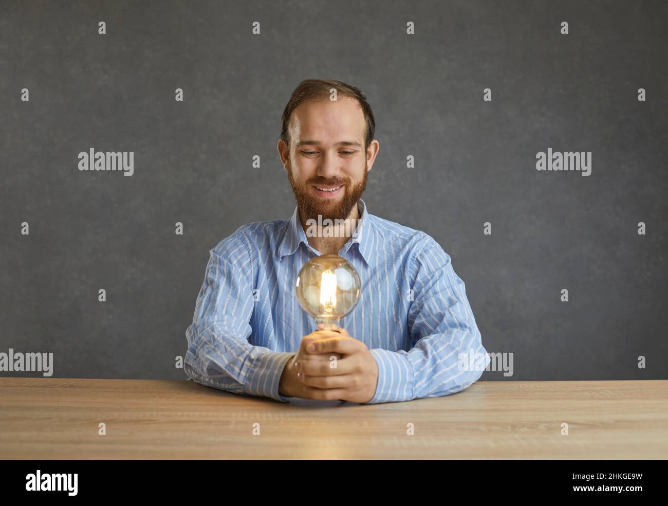 Happy bearded man holding a yellow light bulb sitting at the table on a ...