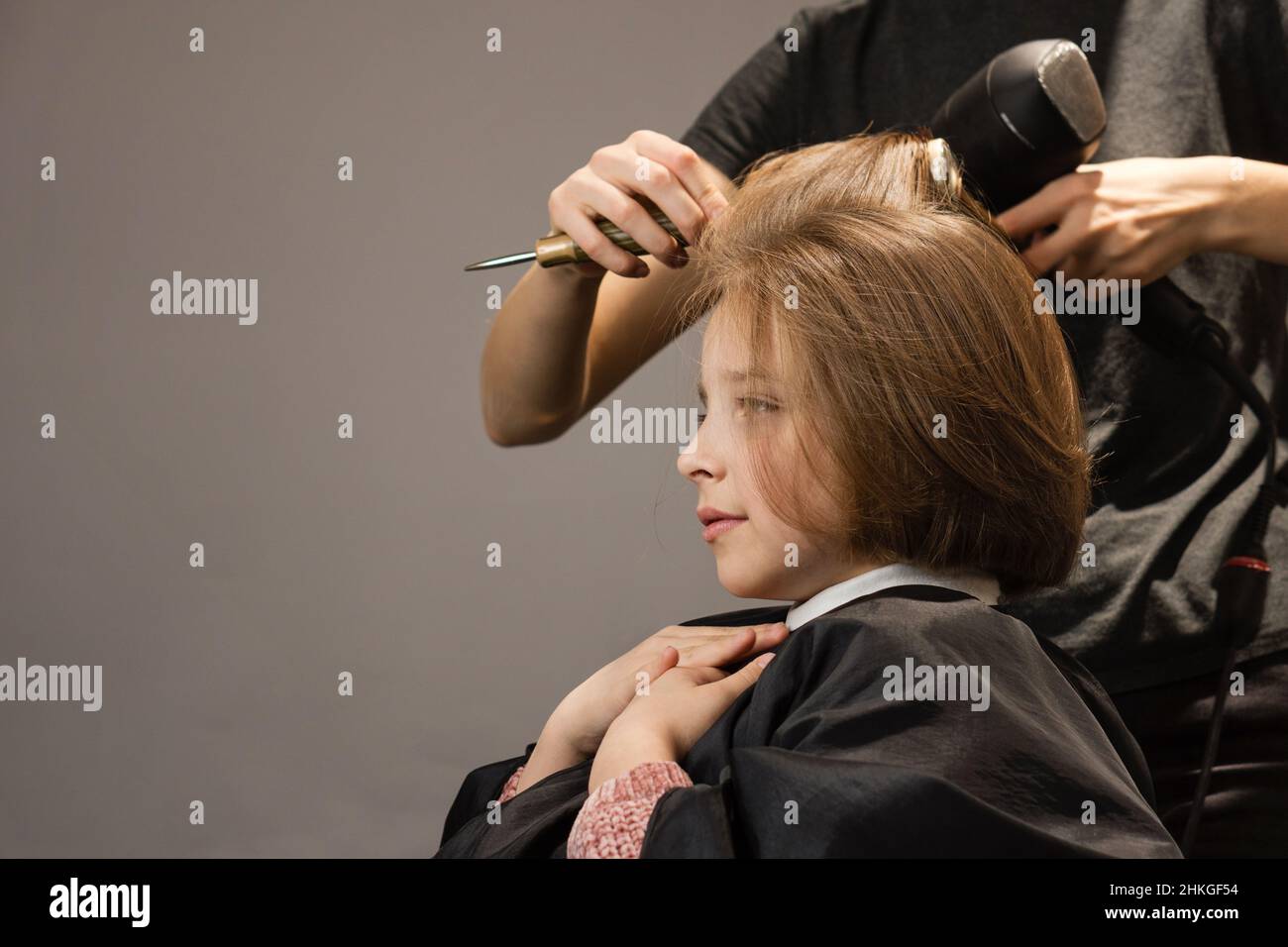 Charming girl enjoys hair care in beauty salon. Child looks in mirror and enthusiastically ...