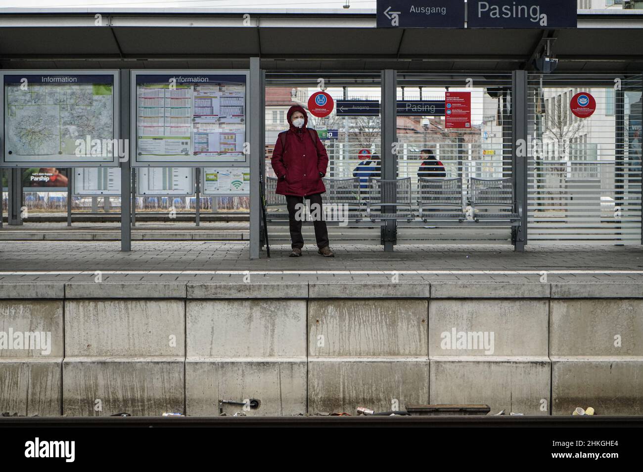 A lady wearing a Covid mask is standing in a waiting area on a platform ...