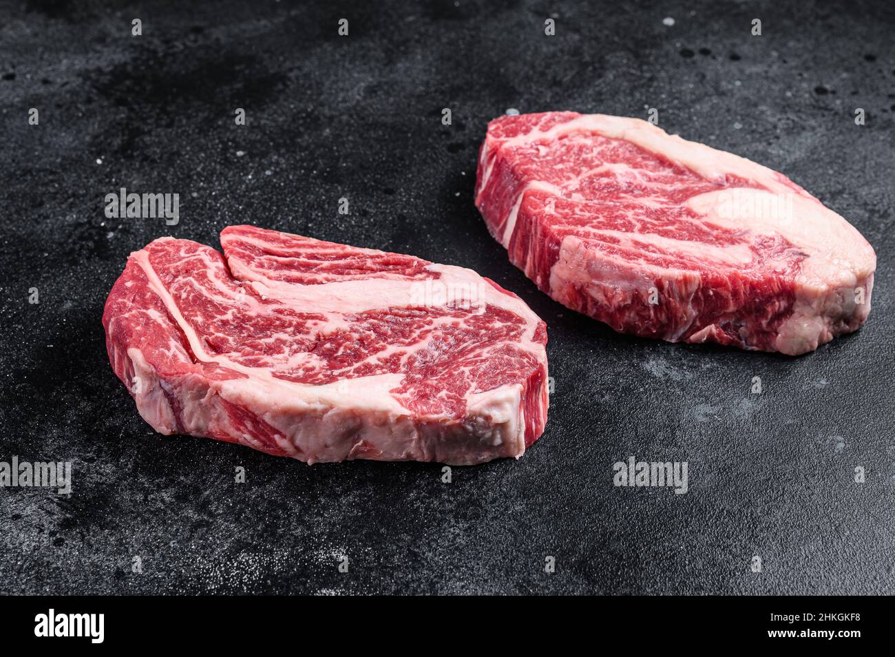 Raw chuck eye roll steaks, premium beef meat on a butcher board. Black ...