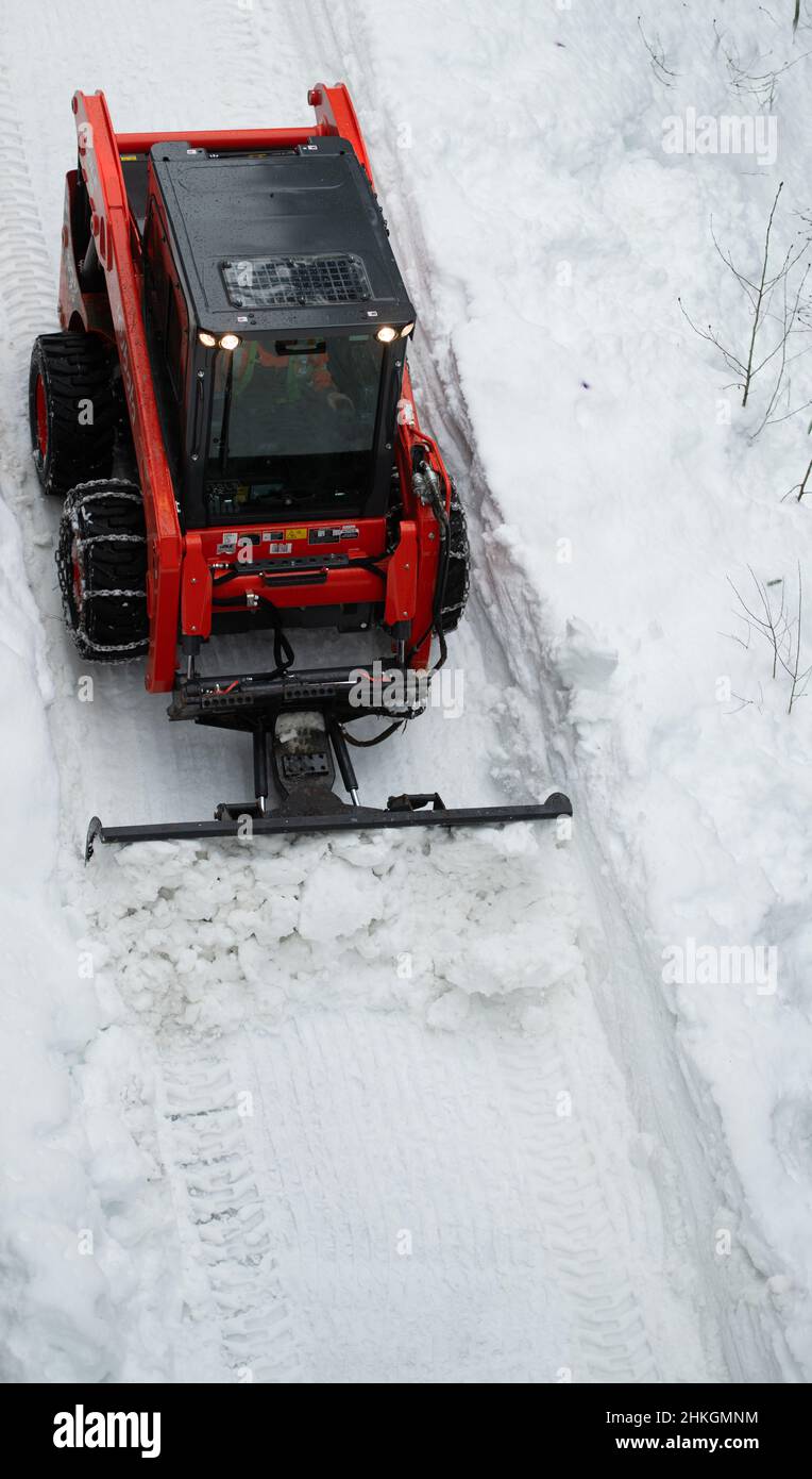 Small snow plow moving snow on walking path as seen from above with ...