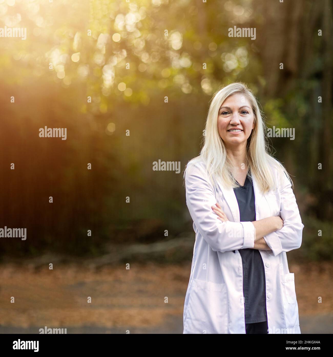 A medical professional with a lab coat with long blond hair outside in ...