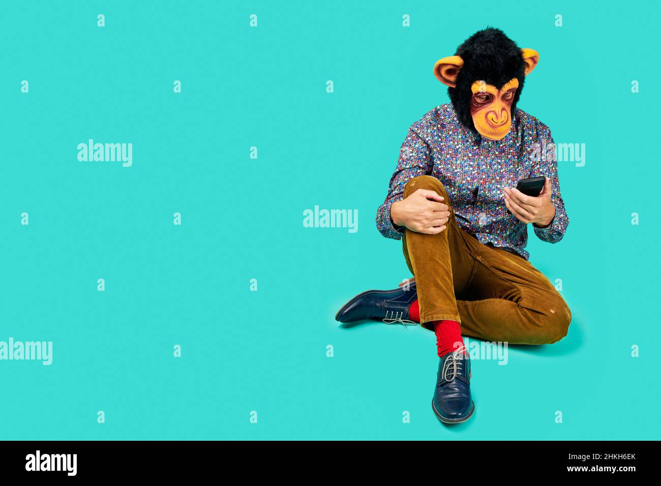 a young man wearing a monkey mask and colorful clothes, sitting on the ...