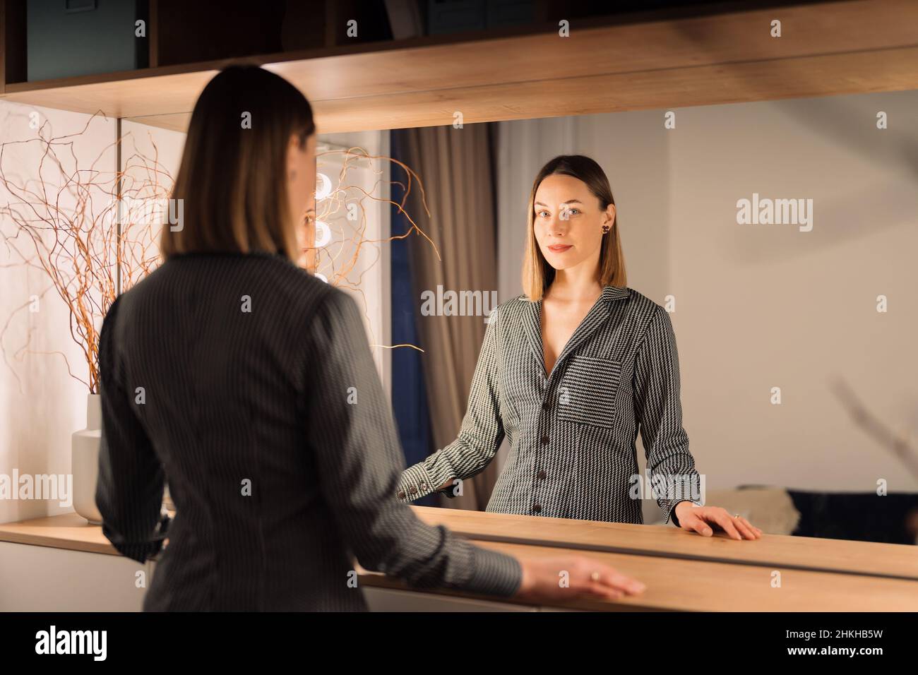 Self-confident Woman looking at her reflection into the mirror indoors ...