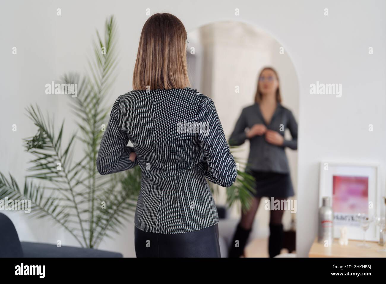 Self-confident Woman looking at her reflection into the mirror indoors ...