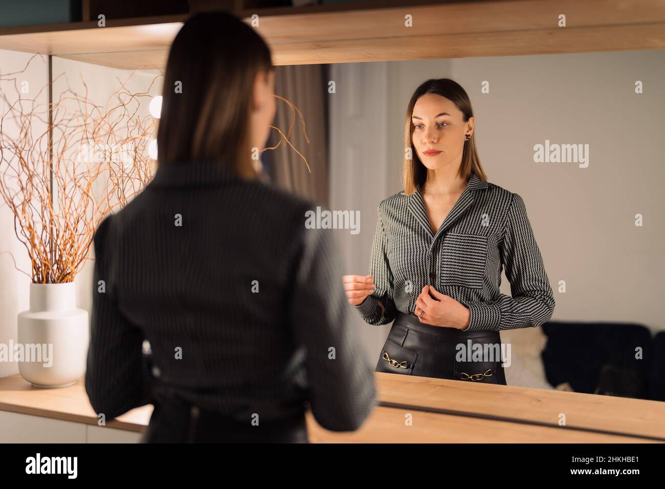 Self-confident Woman looking at her reflection into the mirror indoors ...