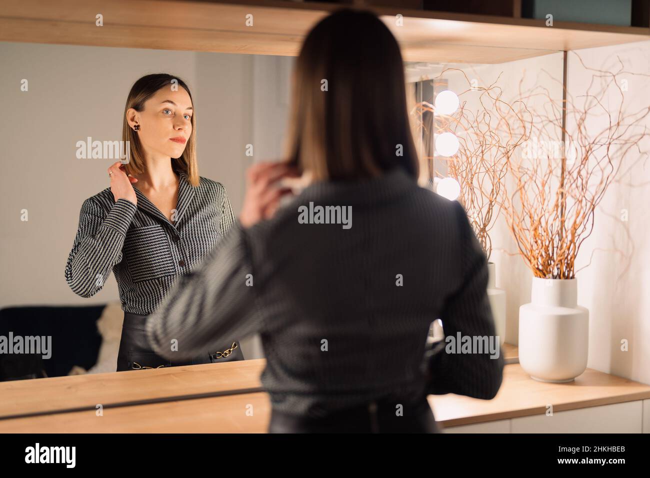 Self-confident Woman looking at her reflection into the mirror indoors ...