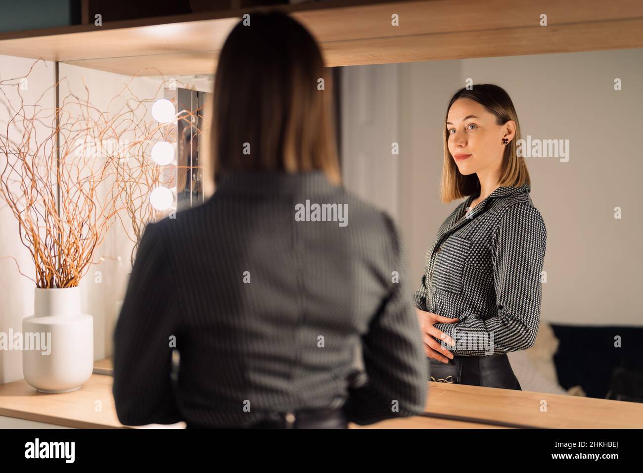 Self-confident Woman looking at her reflection into the mirror indoors ...