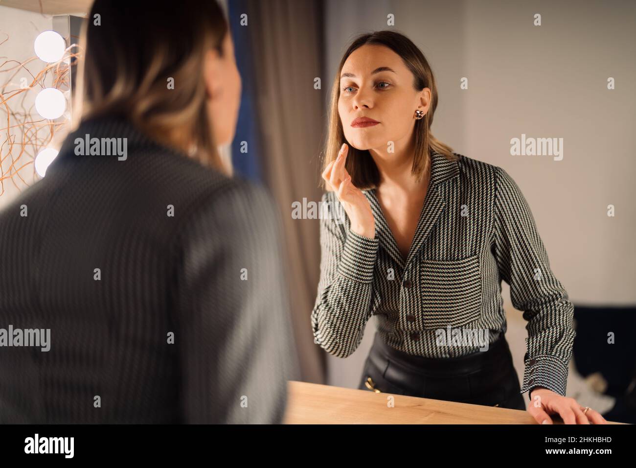 Self-confident Woman looking at her reflection into the mirror indoors ...