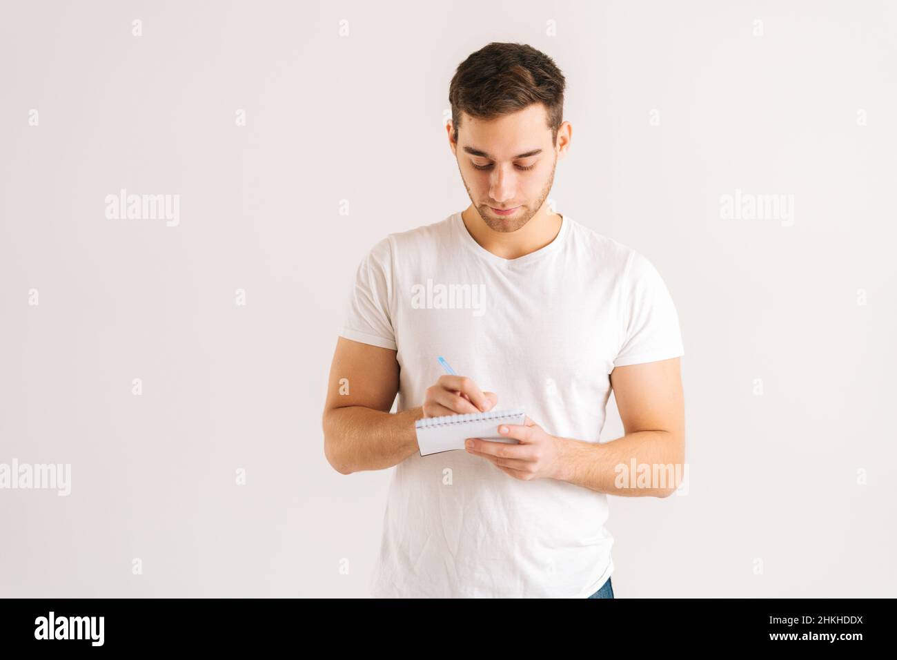 Studio portrait of handsome young man writing in copybook with pen ...